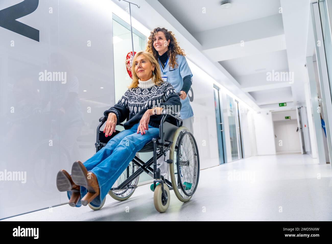Nurse smiling while pushing a wheelchair with a injured woman along the ...