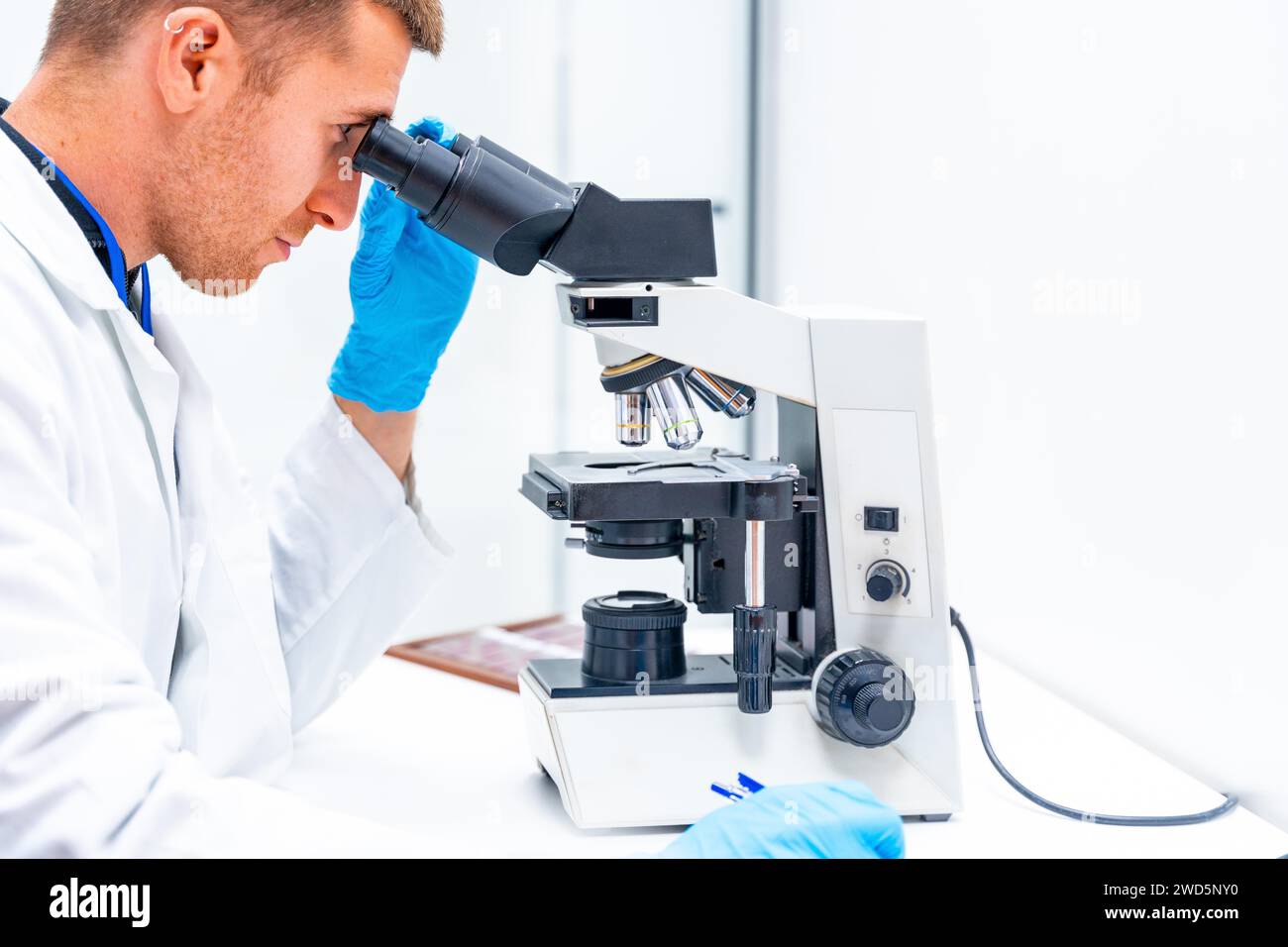 Side close-up view of a male young doctor using microscope to analyze ...