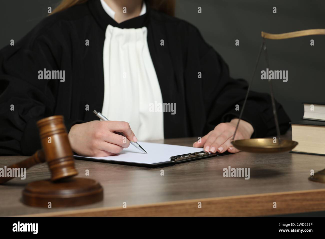 Judge with pen and clipboard working at wooden table in courtroom ...