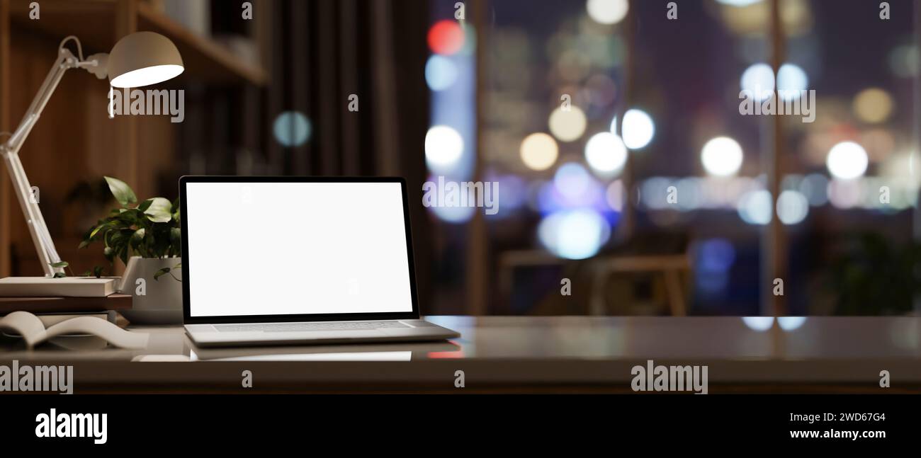 Modern office desk at night in a dark room with a white-screen laptop ...