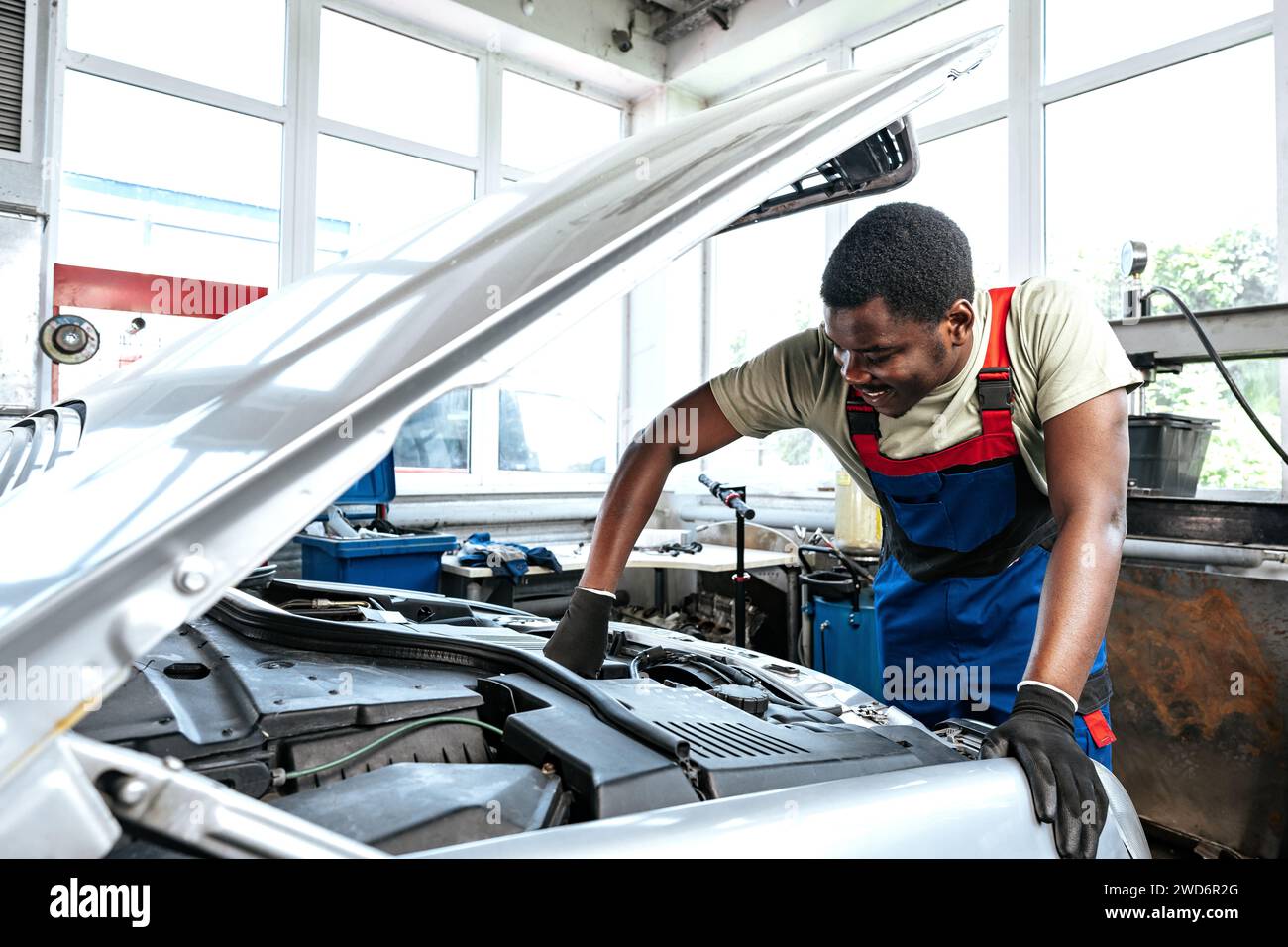 Young African man working under the hood of car fixing engine in auto ...