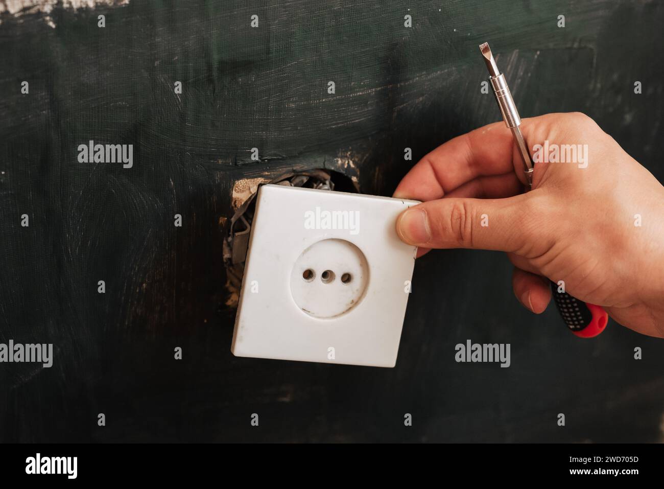 male electrician removes an old electrical outlet with a screwdriver ...