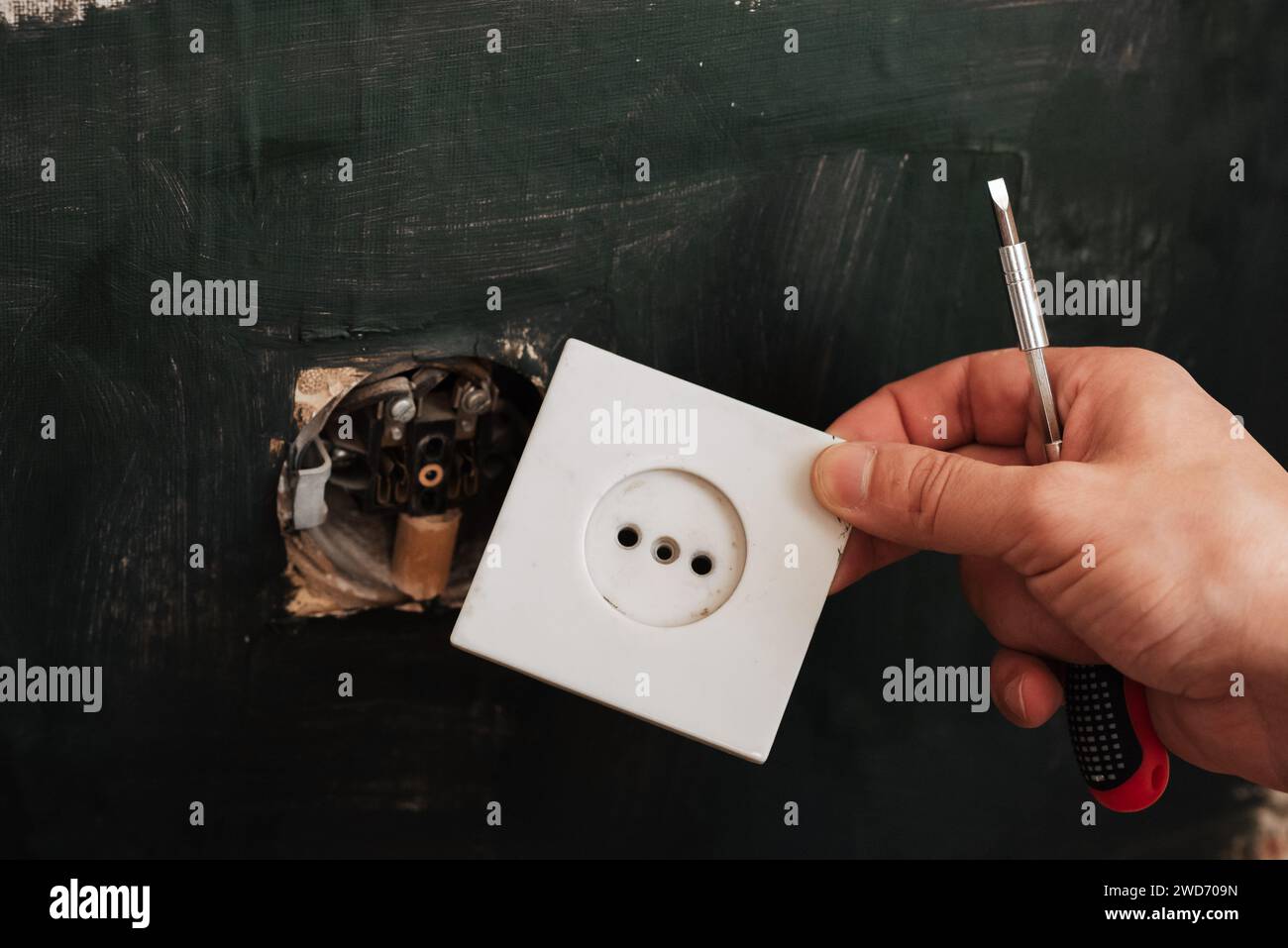 male electrician removes an old electrical outlet with a screwdriver ...