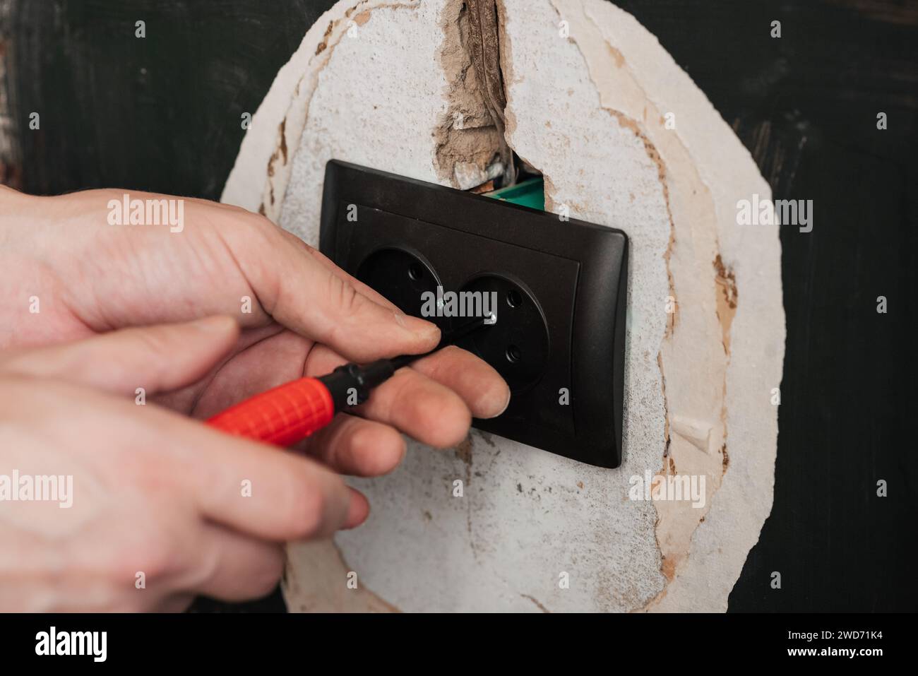 male electrician replaces and installs a new electrical outlet with his ...