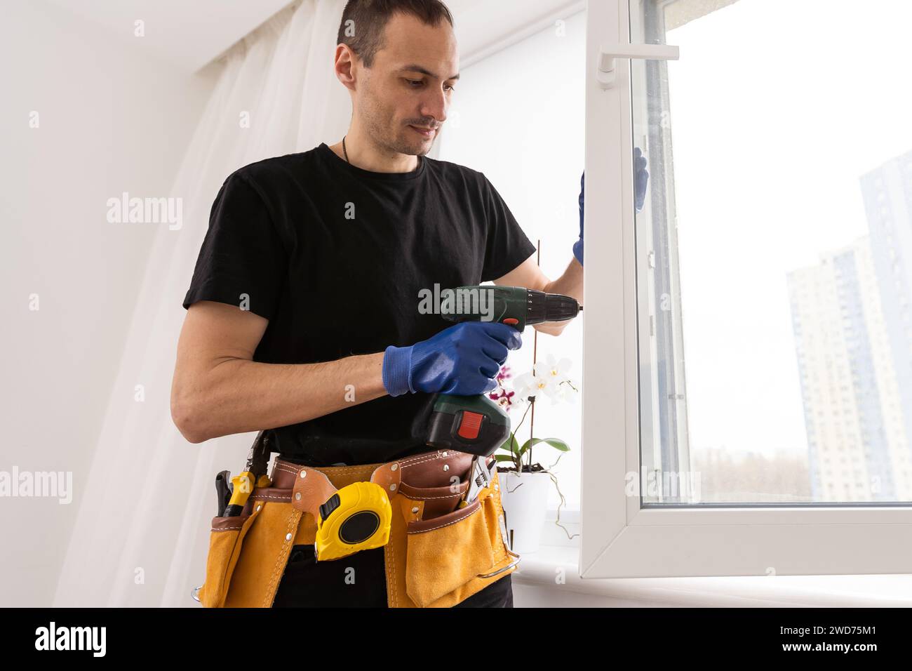 Handyman using a cordless screwdriver to install a window handle ...