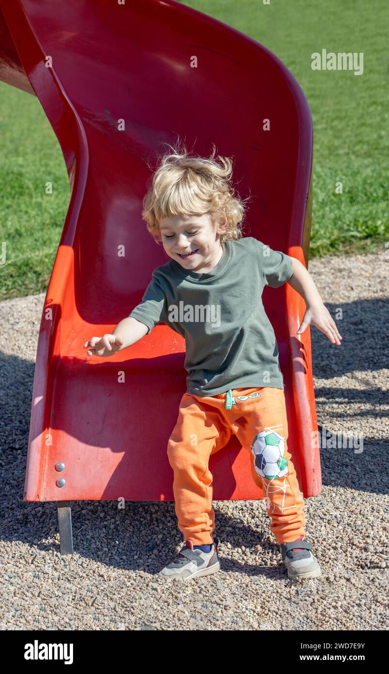 A cheerful boy jumped to the ground after slipping on a slide Stock ...