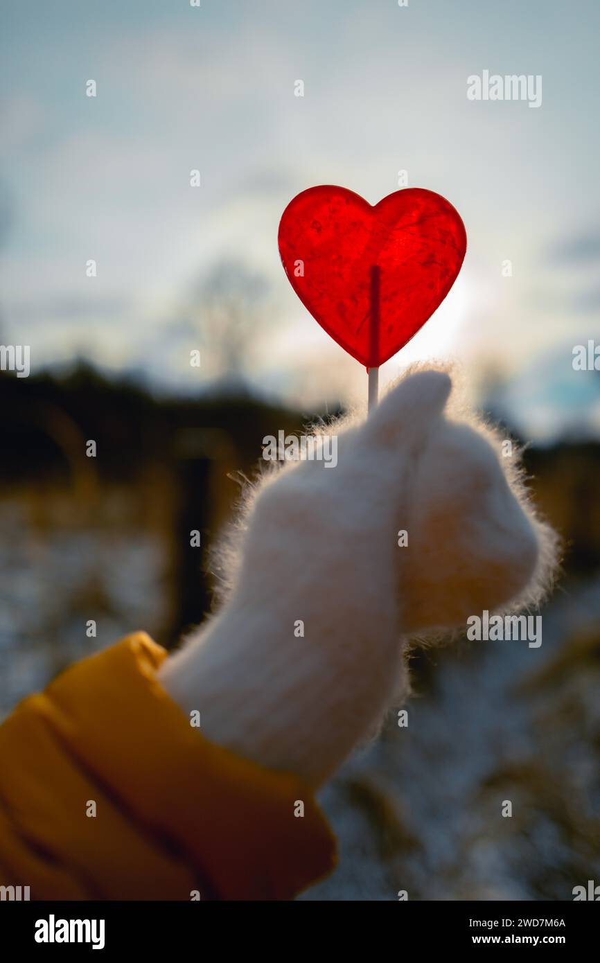 Woman's hand in a fluffy white mitten holding heart shaped lollipop ...