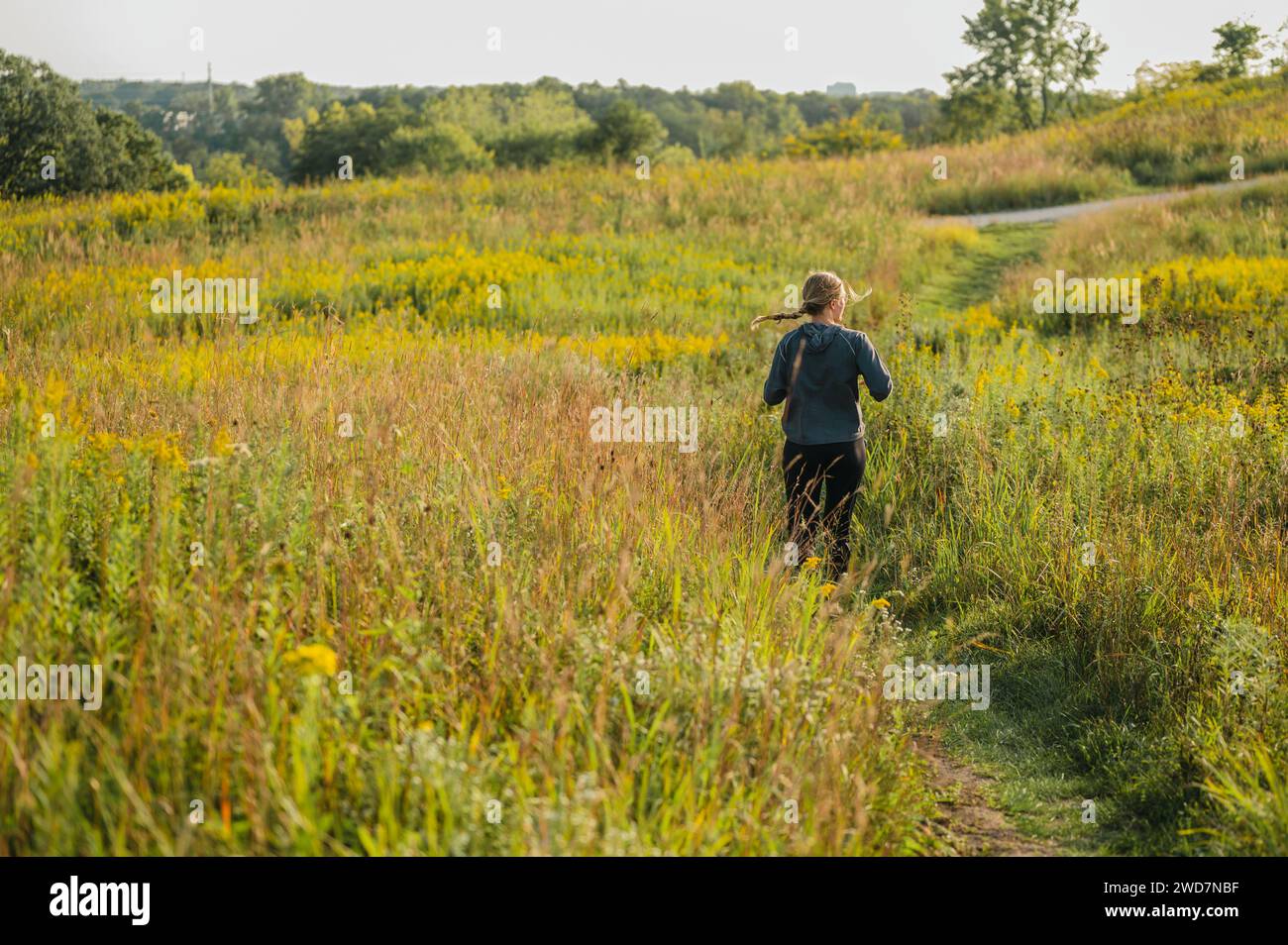 Woman running on prairie path with green foliage and wildflowers Stock ...