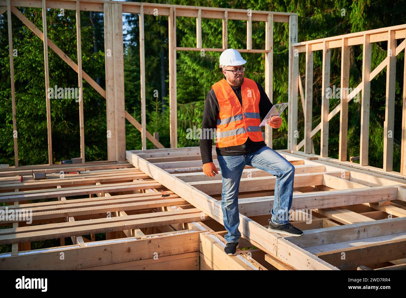 Engineer building wooden two-story structure near woods. Bearded with ...