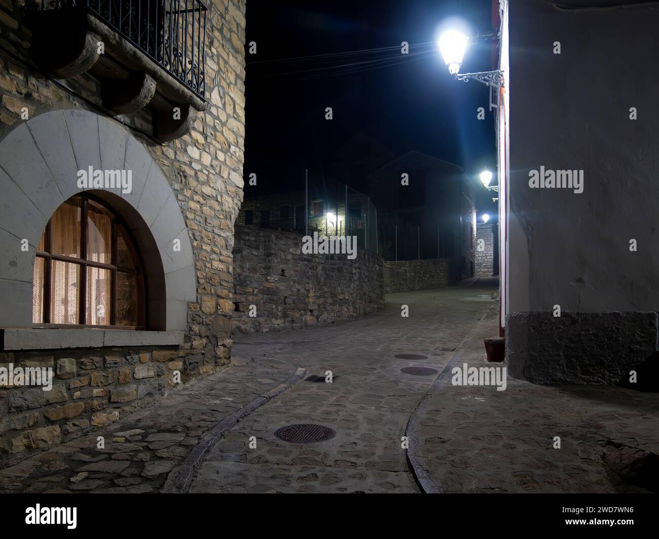 quiet, dimly lit street at night with stone buildings, an arched window ...