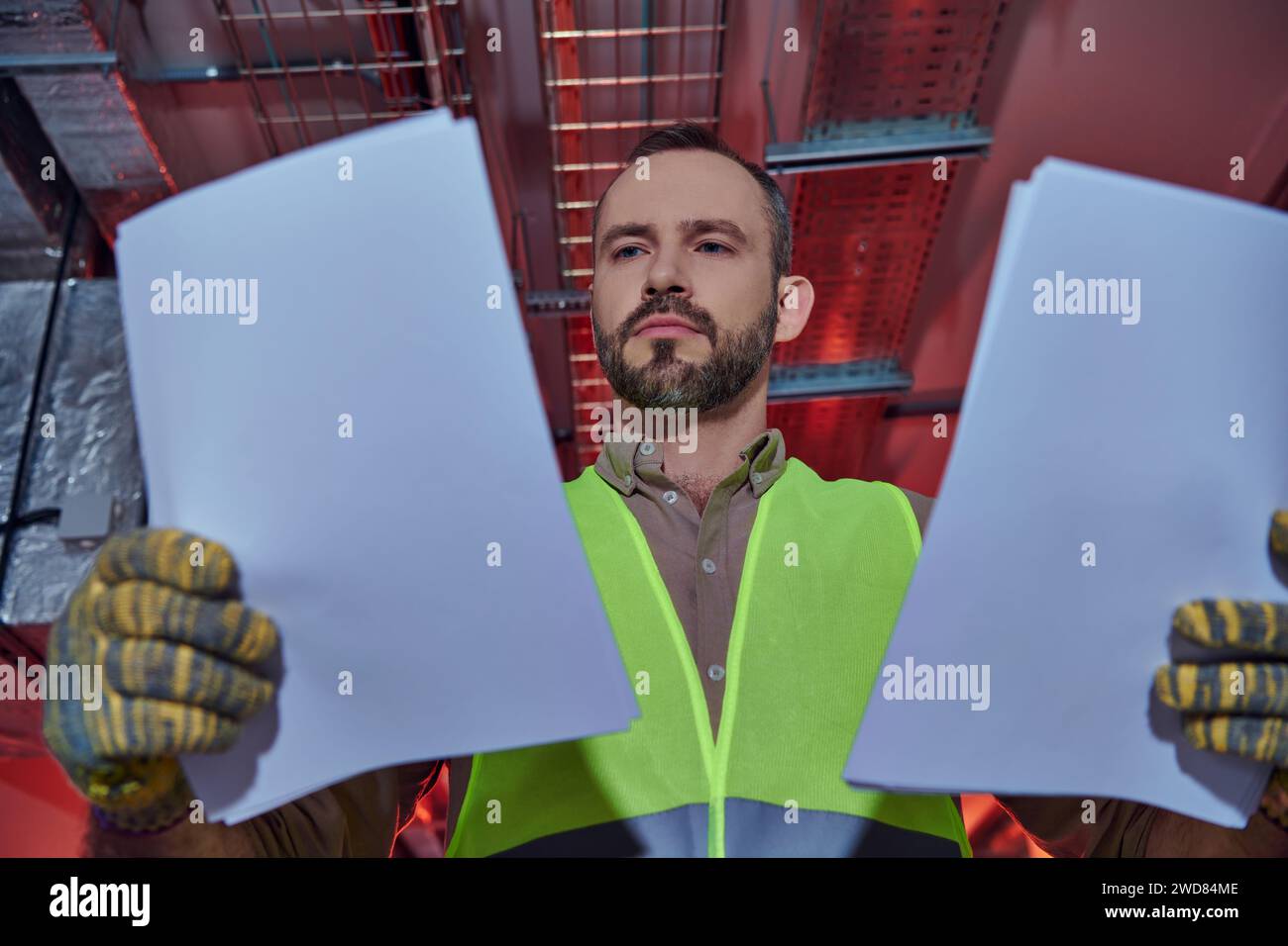 good looking hardworking professional in safety clothes looking at his ...