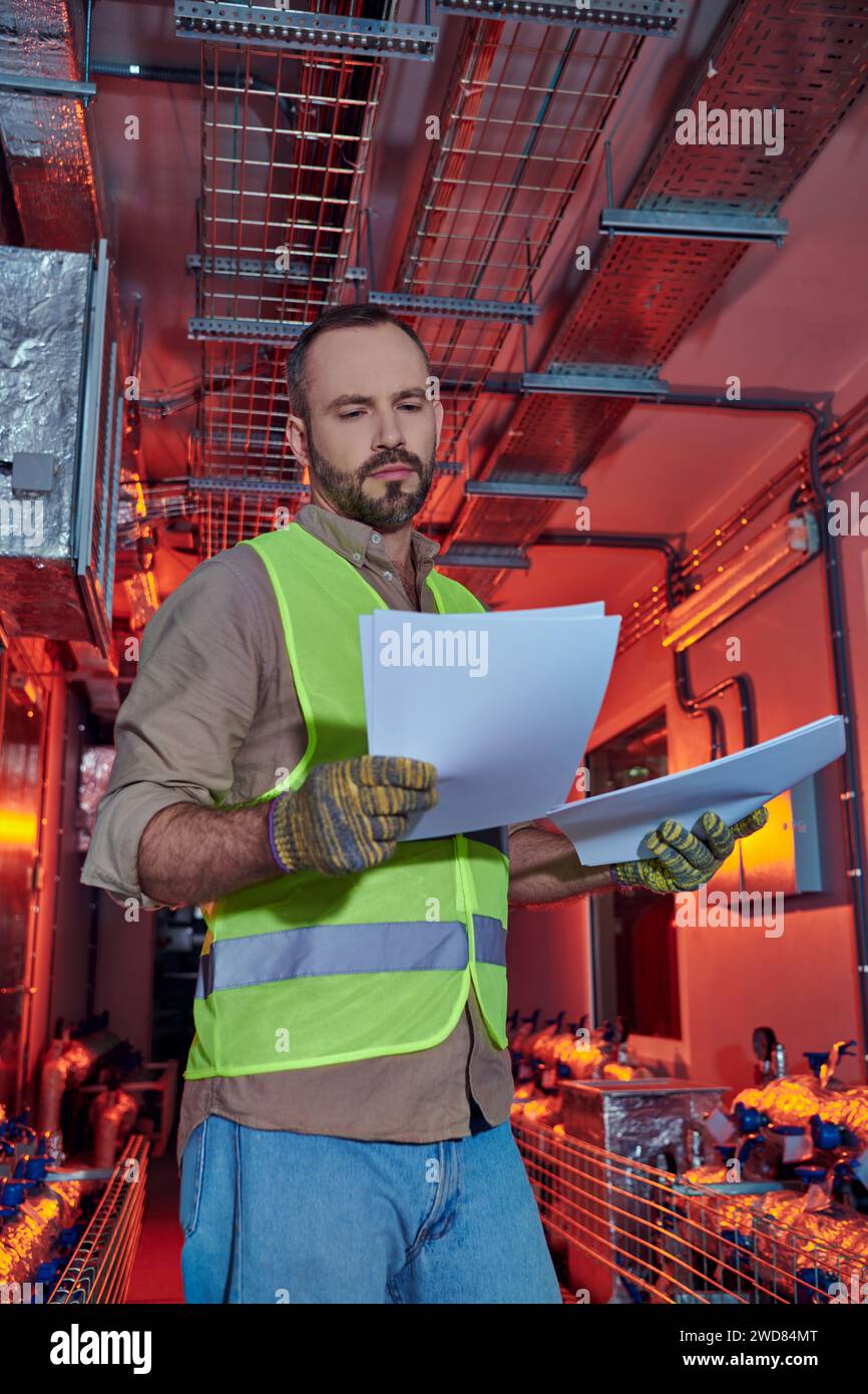 handsome focused specialist in safety gloves and vest looking at his ...