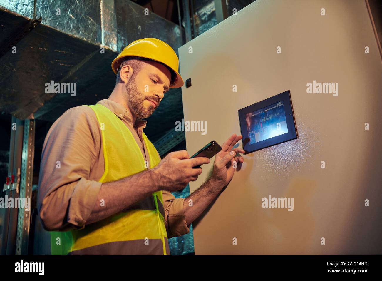 good looking pensive technician in safety clothes and helmet looking at ...