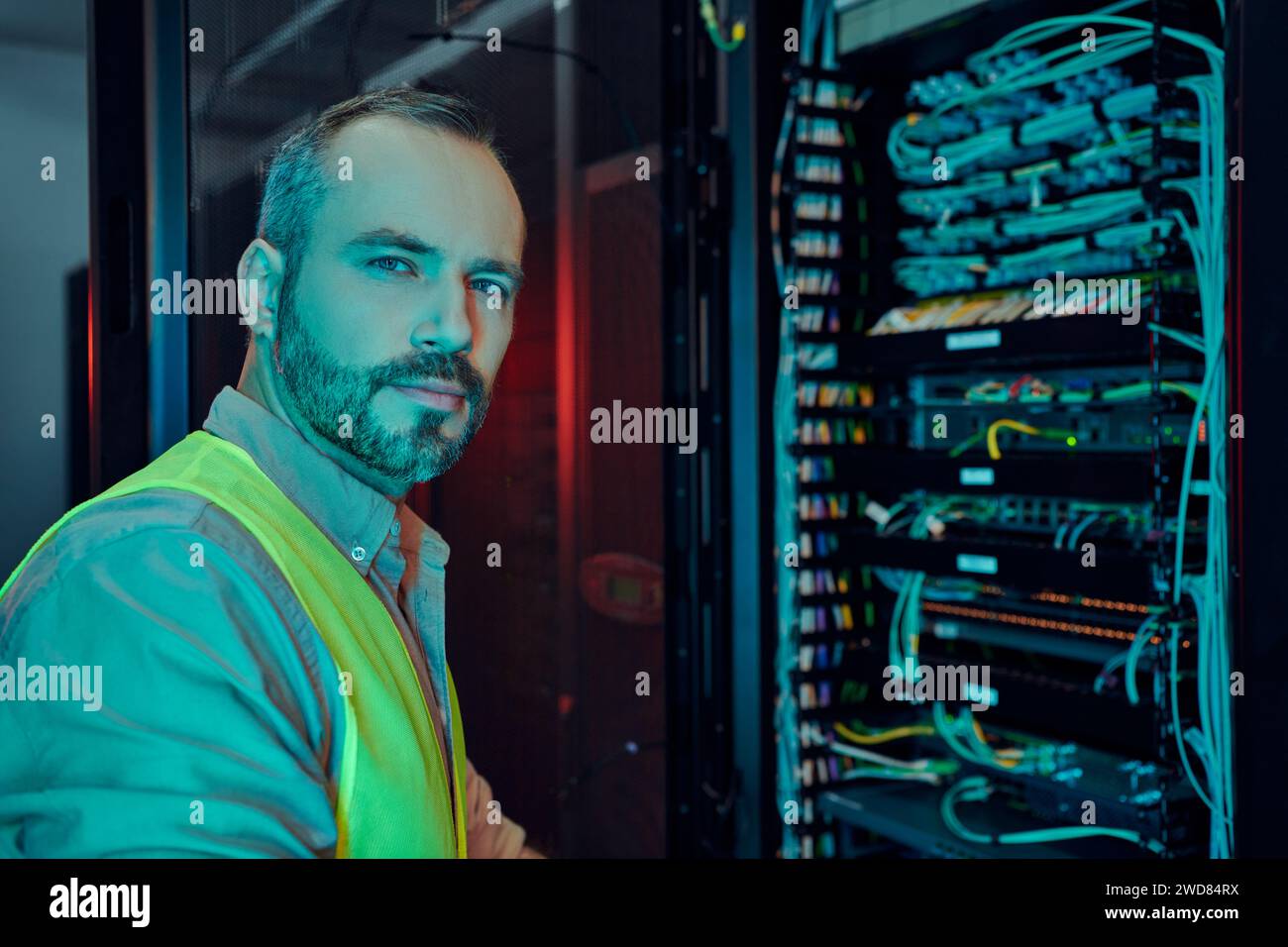 attractive pensive man with beard in safety vest inspecting data center ...