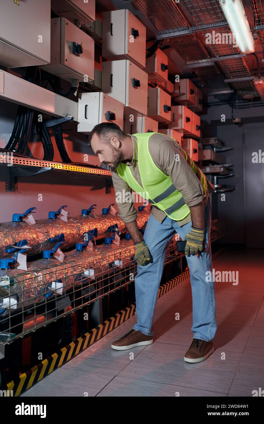 attractive concentrated technician in safety gloves and vest leaning ...