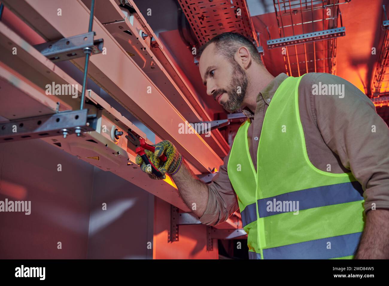 handsome focused professional in safety vest and gloves using pliers ...