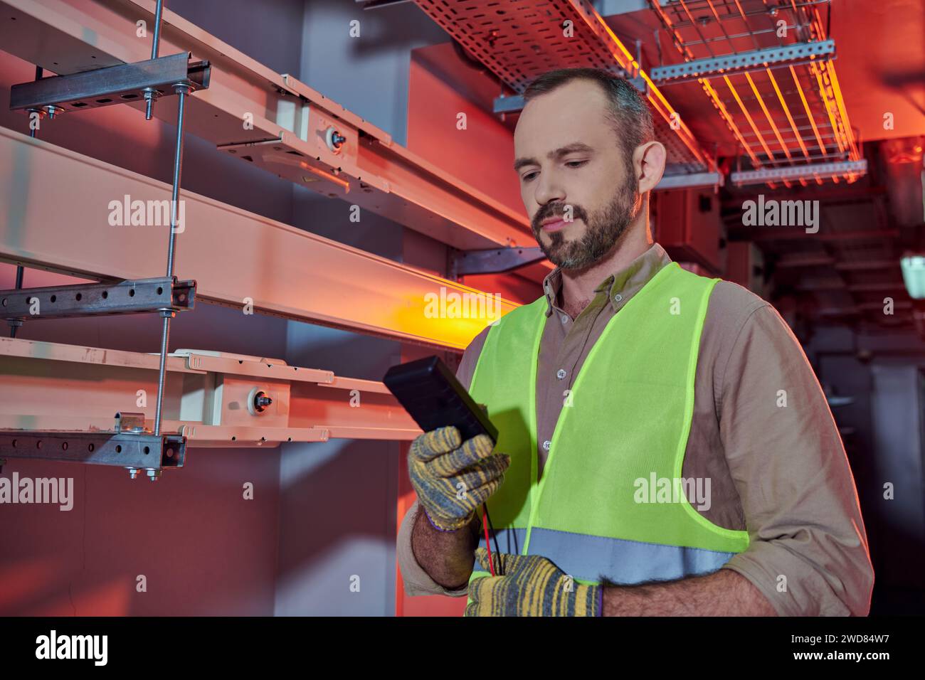 cheerful handsome technician in safety vest and gloves looking at his ...