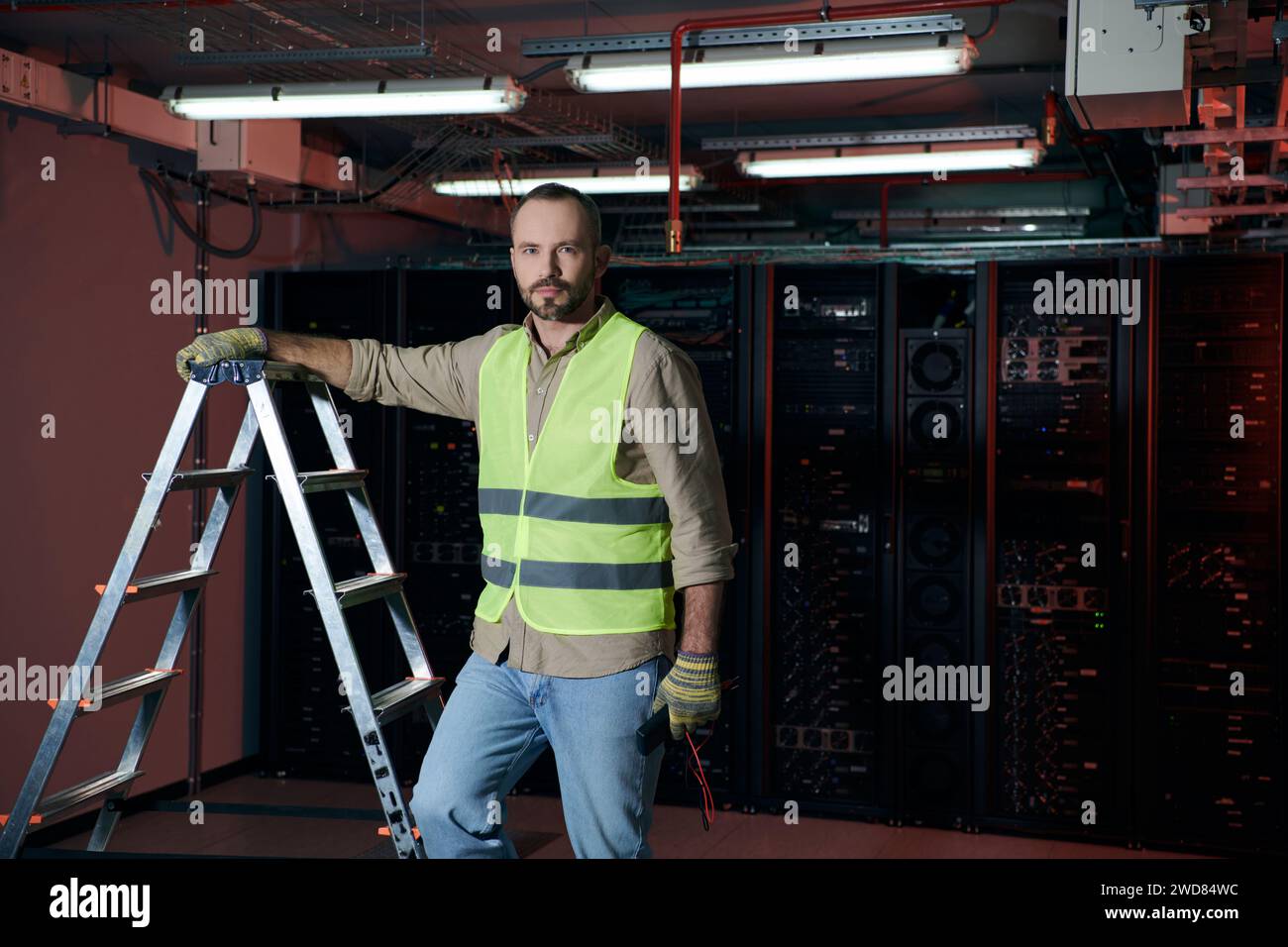good looking technician in safety vest and gloves standing next to step ...
