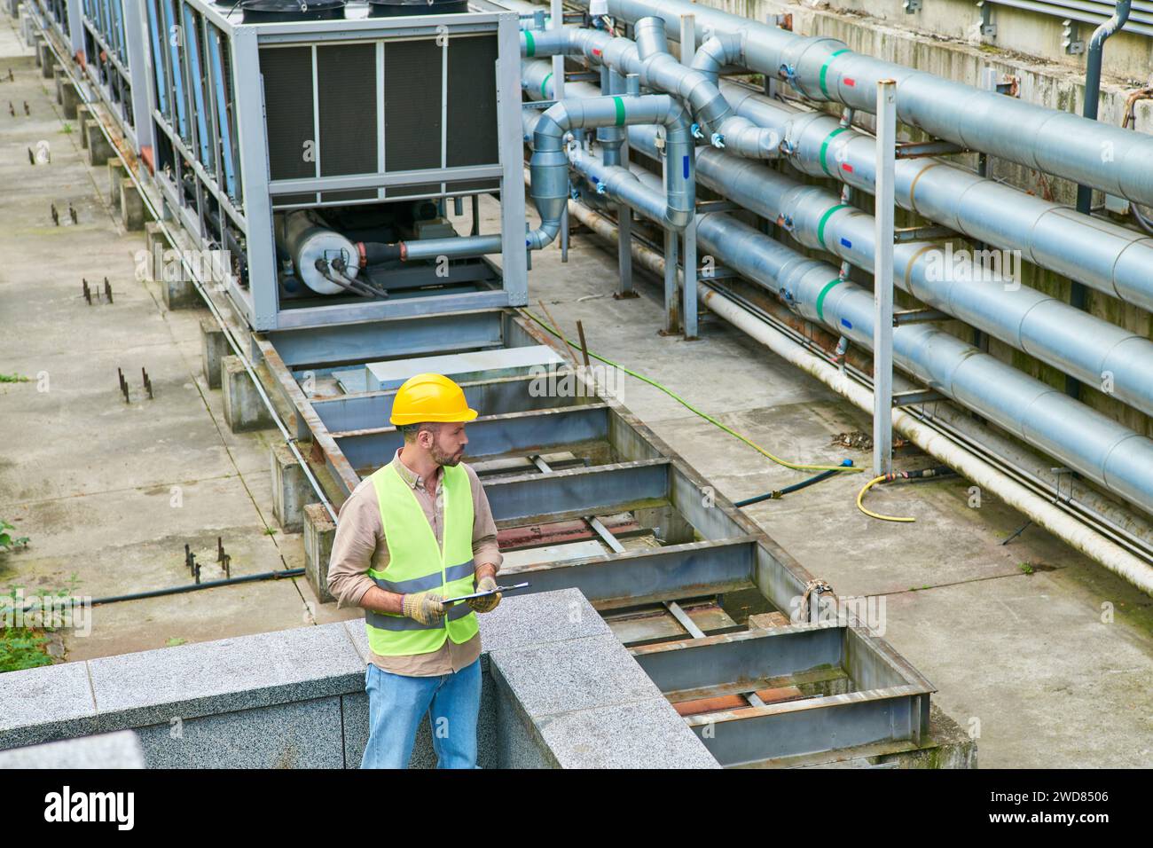 handsome focused technician in safety vest and helmet posing with ...