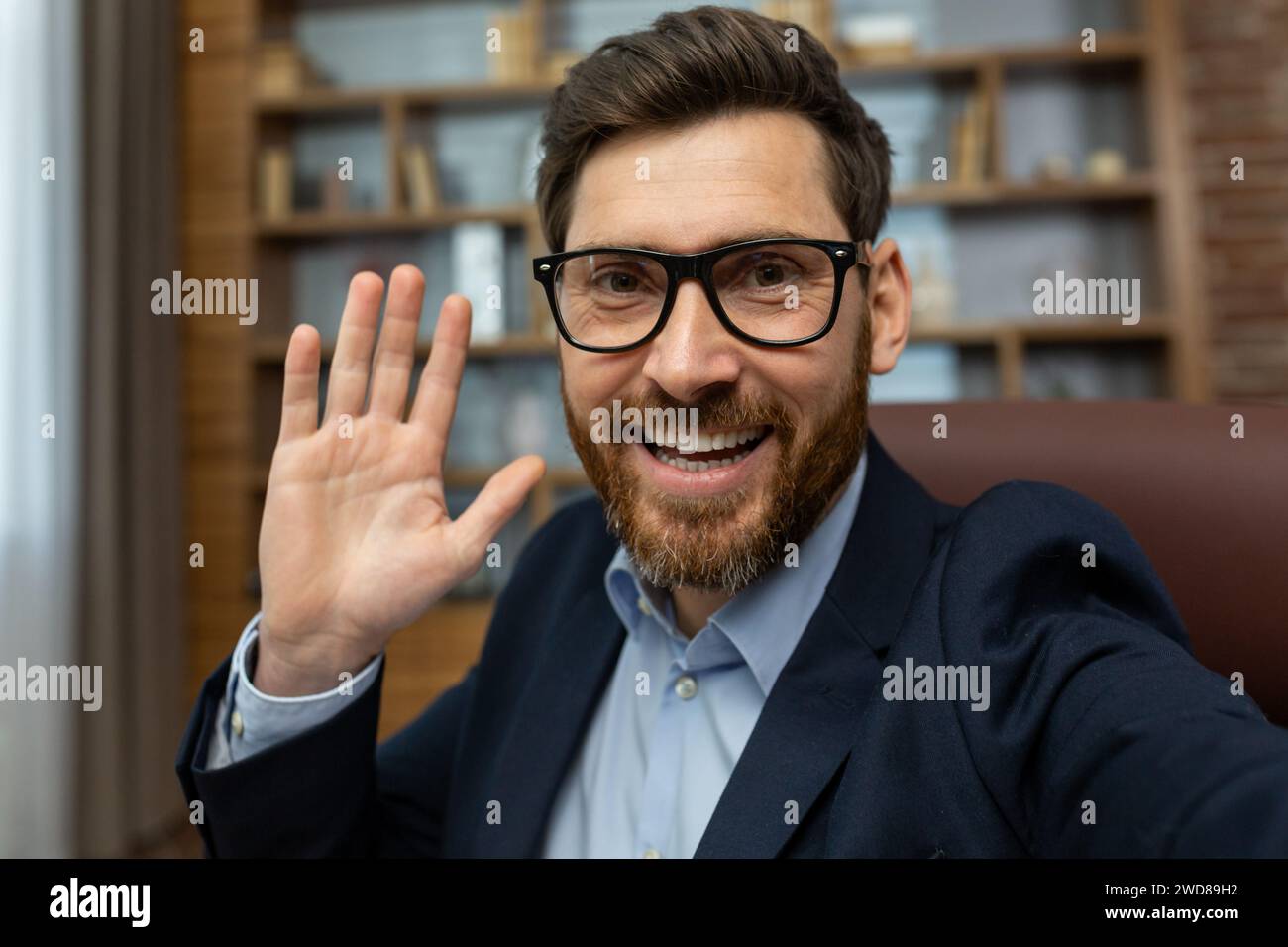 Friendly mature businessman with glasses waving hello, working from a ...