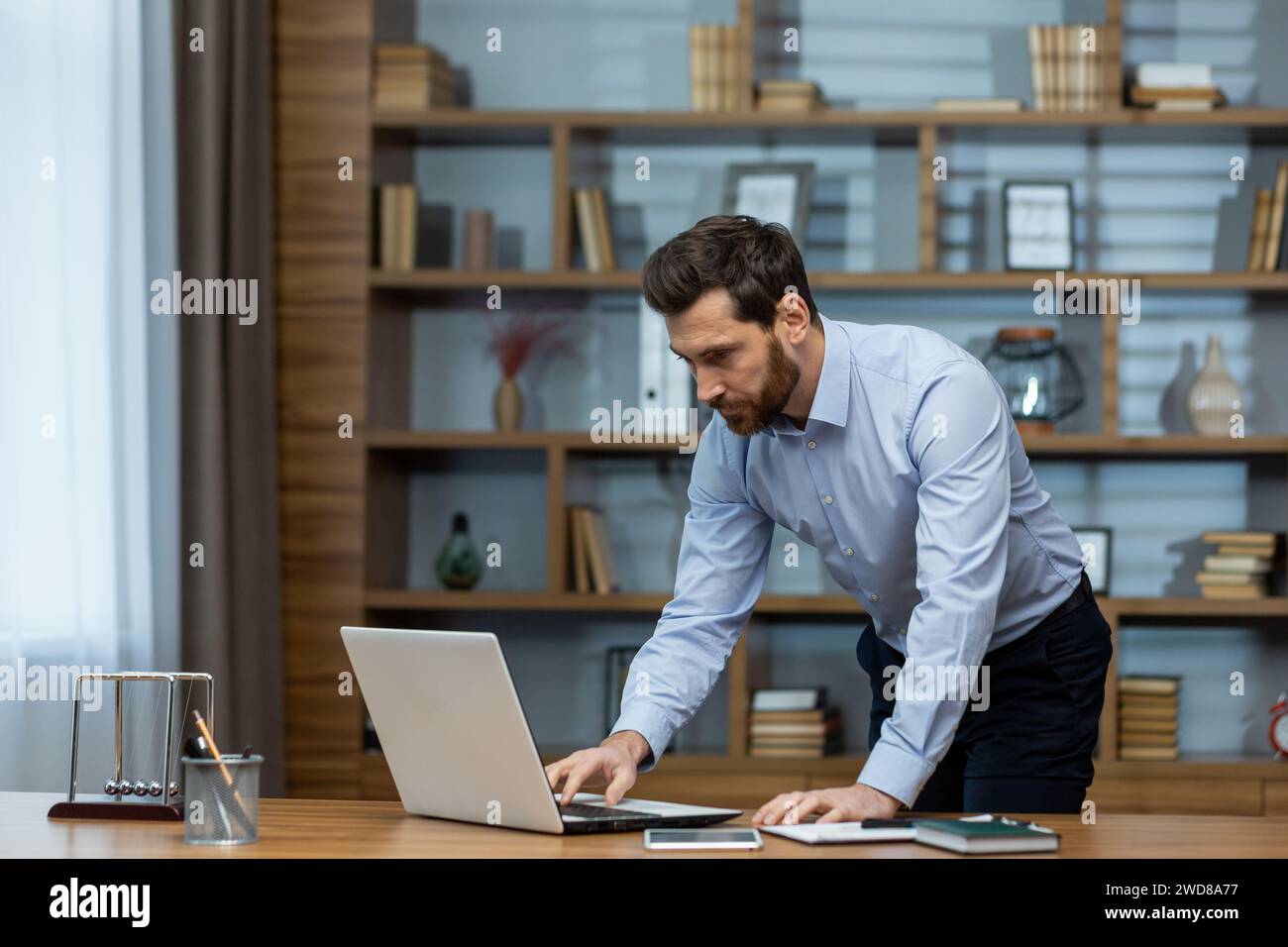 Focused mature businessman reviewing documents at his laptop in a well ...