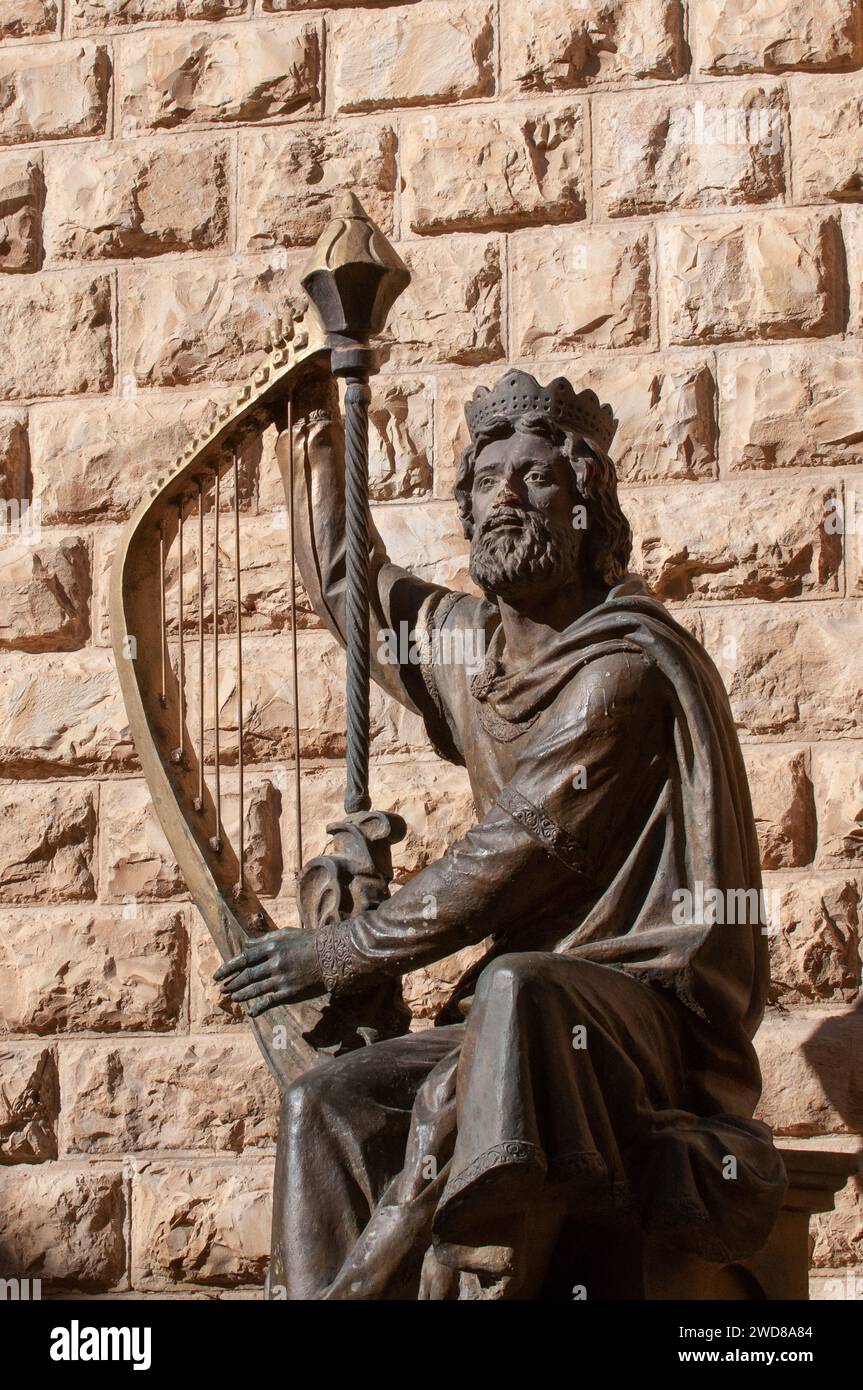 Bronze statue of King David beside a stone wall playing the harp ...