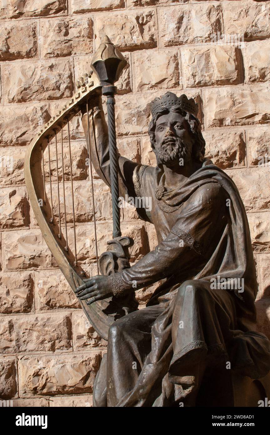 Bronze statue of King David beside a stone wall playing the harp ...
