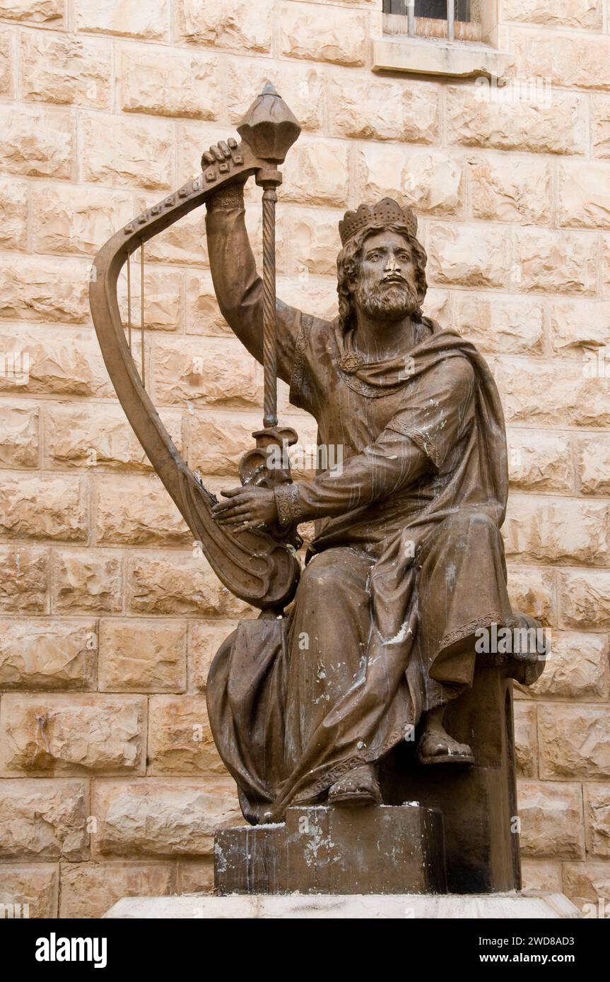 Bronze statue of King David beside a stone wall playing the harp ...
