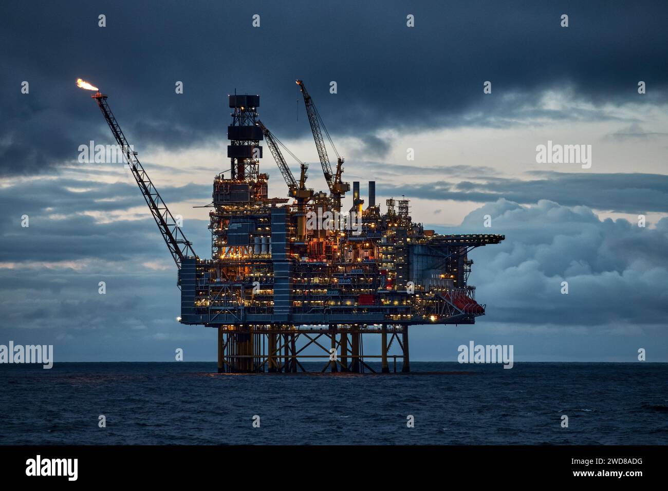 Close up view of illuminated drilling rig at night, with dark blue sky ...