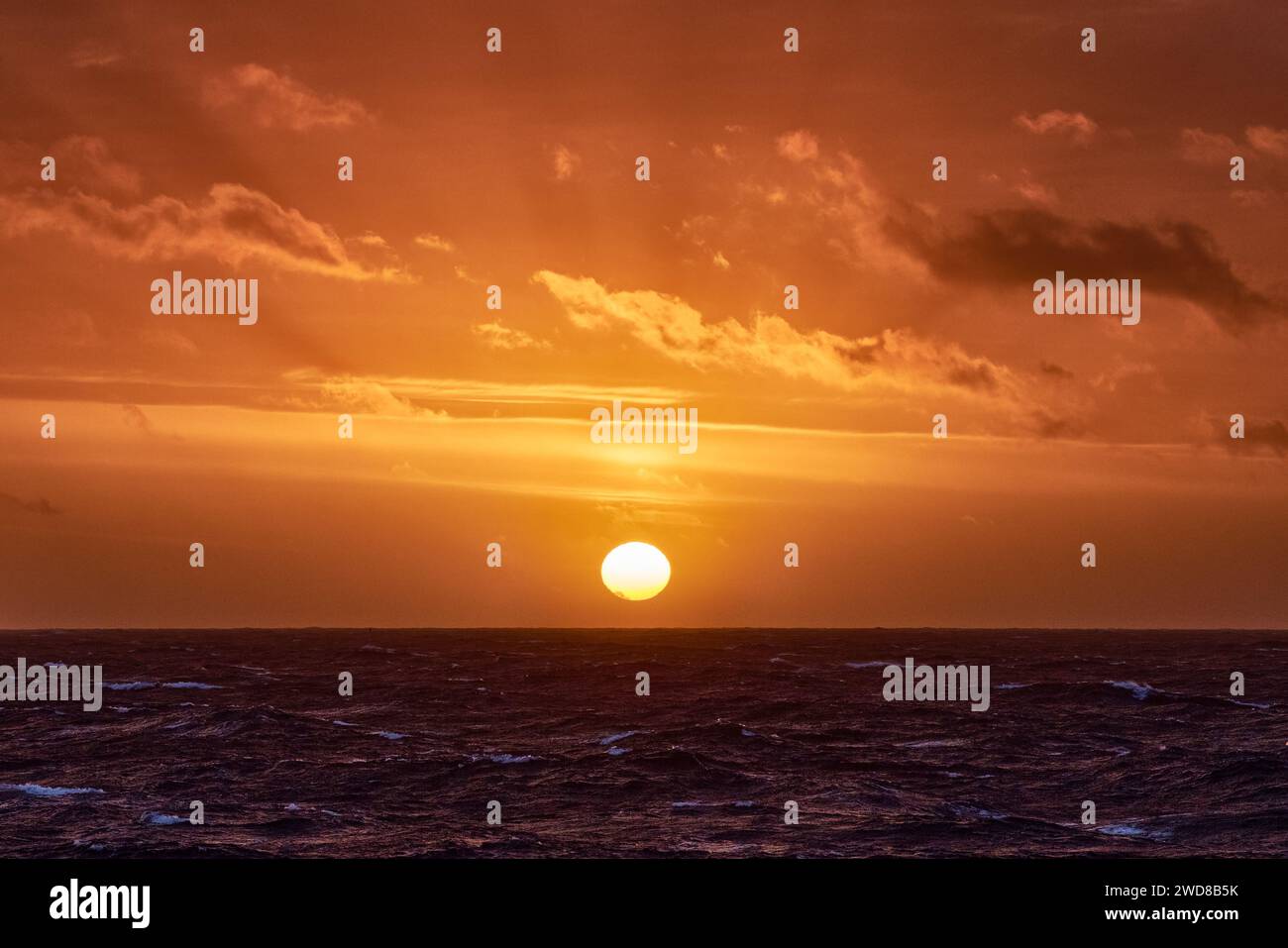 Orange ocean sunset, with clouds, blue ocean and sun on the horizon ...