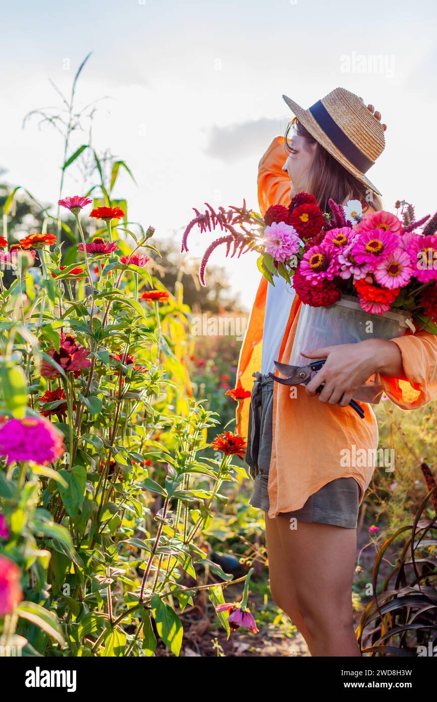 Portrait of woman farmer picking flowers in bucket in summer garden at ...