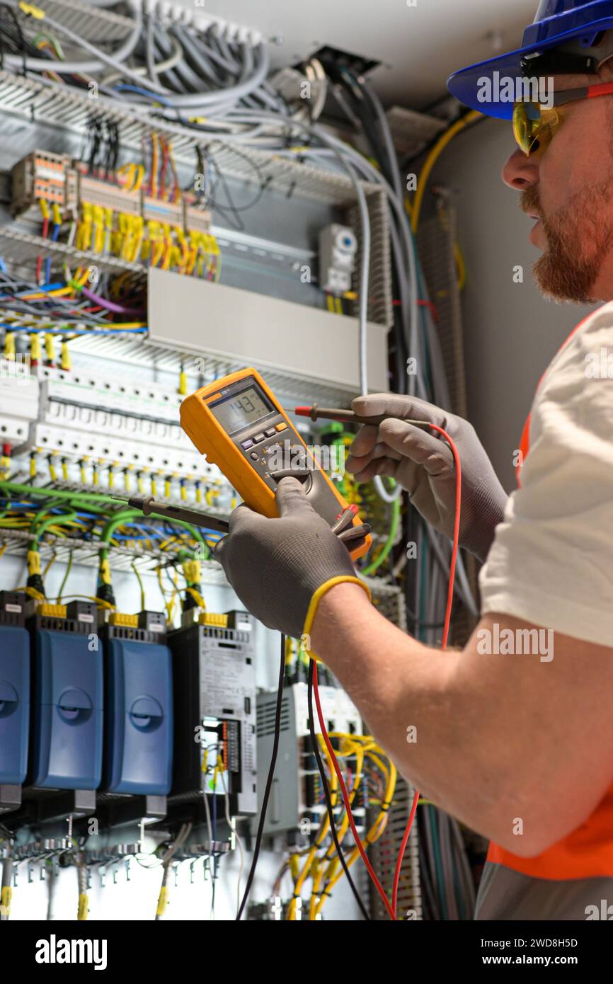 electrician in blue helmet, yellow glasses and orange vest measures ...