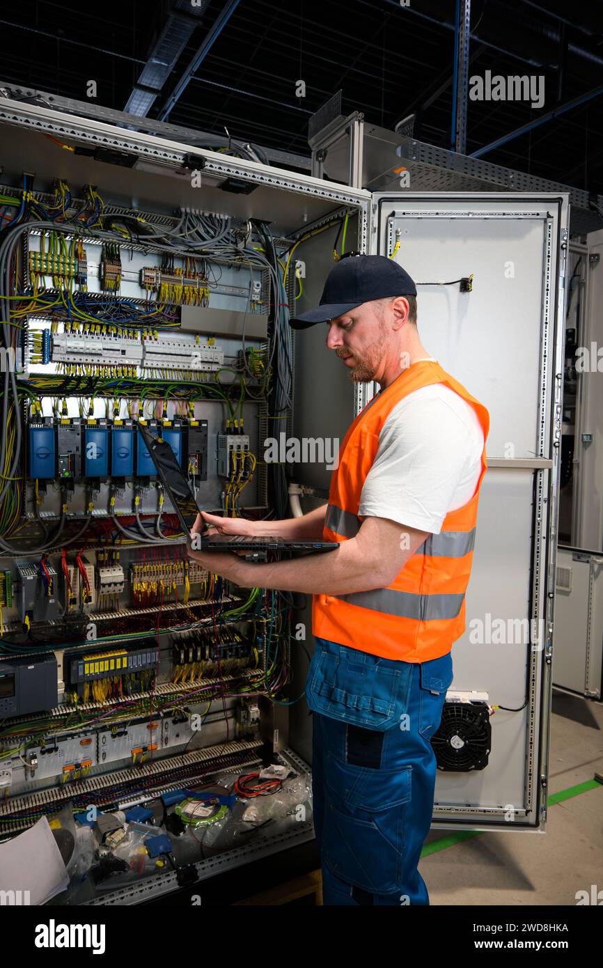 an electrician in a cap and orange vest installs a large electrical ...