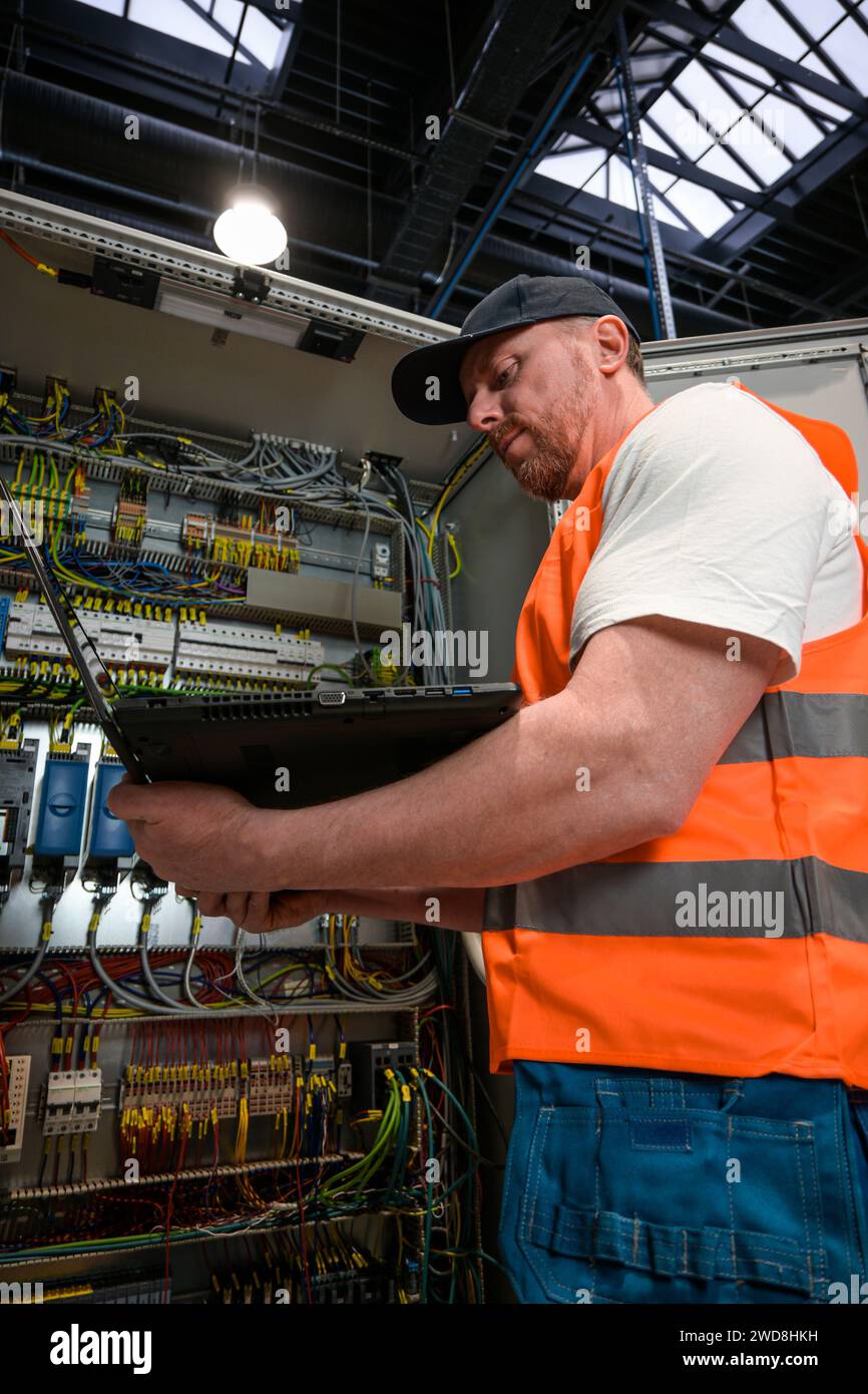 an electrician in a cap and orange vest installs a large electrical ...