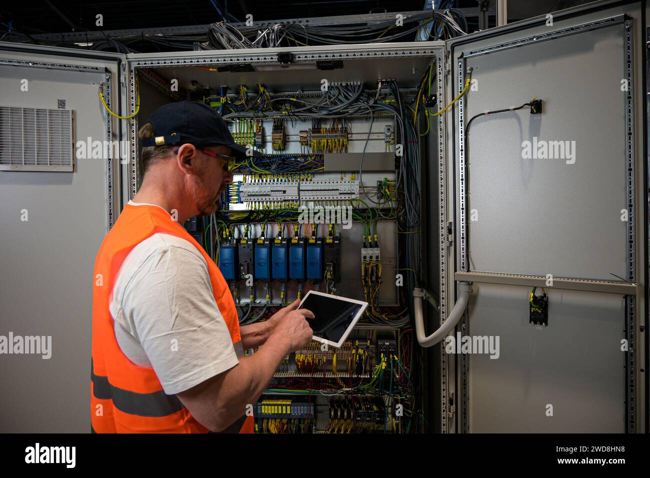 an electrician in a cap and orange vest installs a large electrical ...