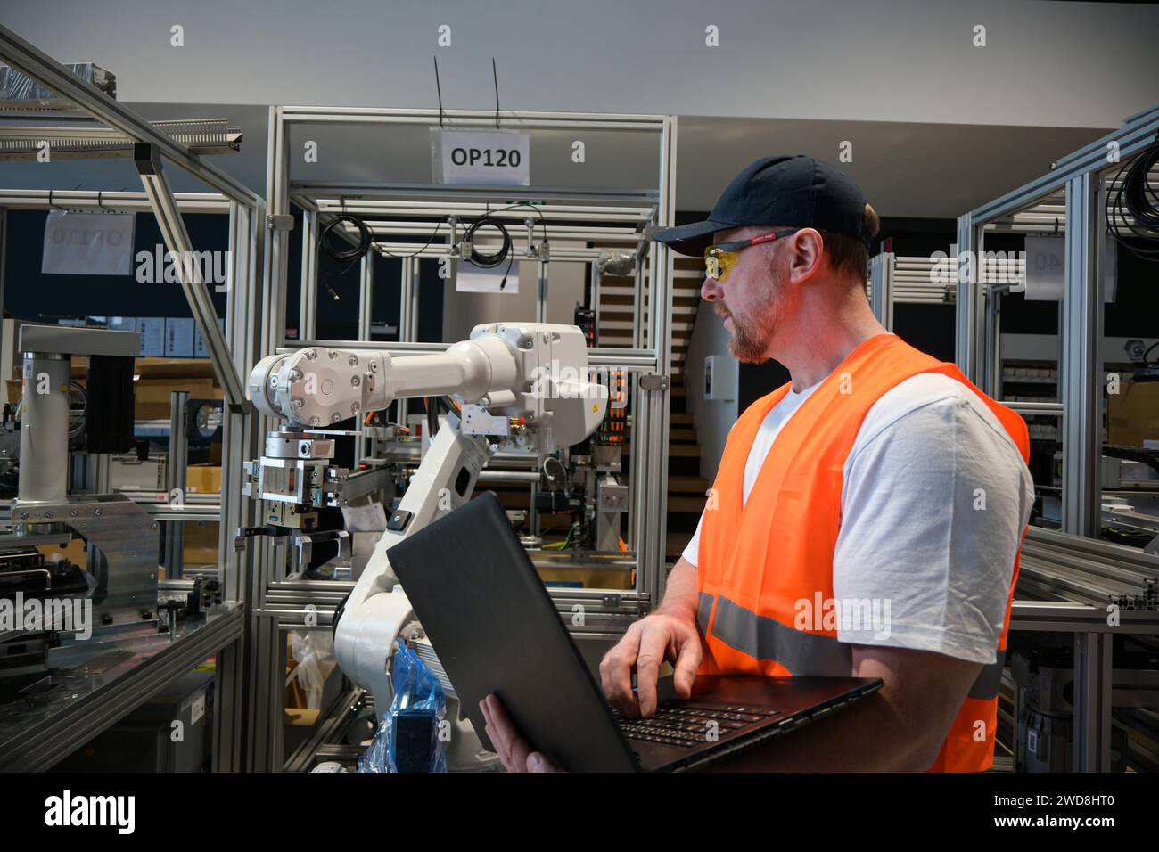 an engineer in a vest is programming a robot on an assembly line using ...