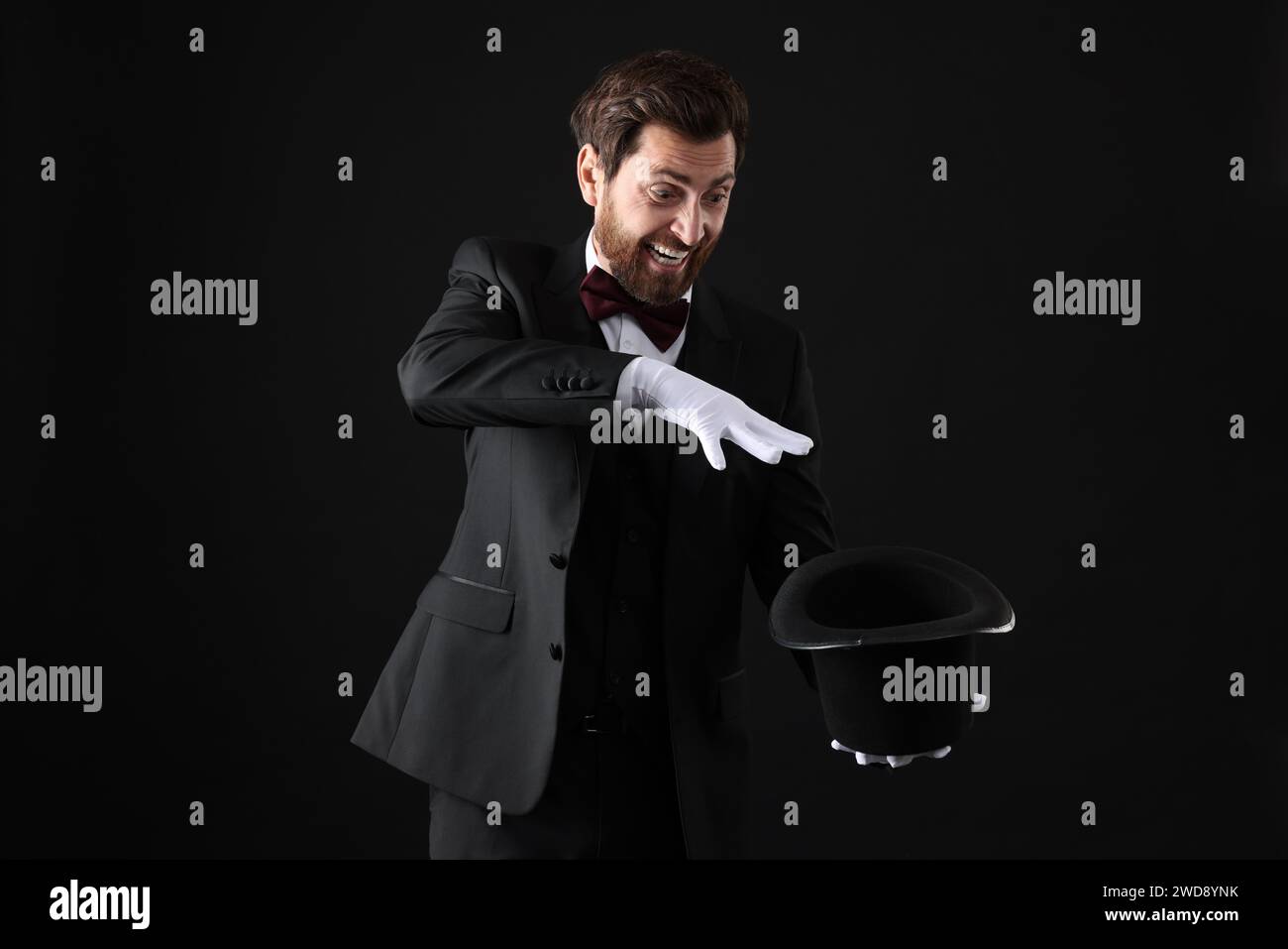 Happy magician showing magic trick with top hat on black background ...