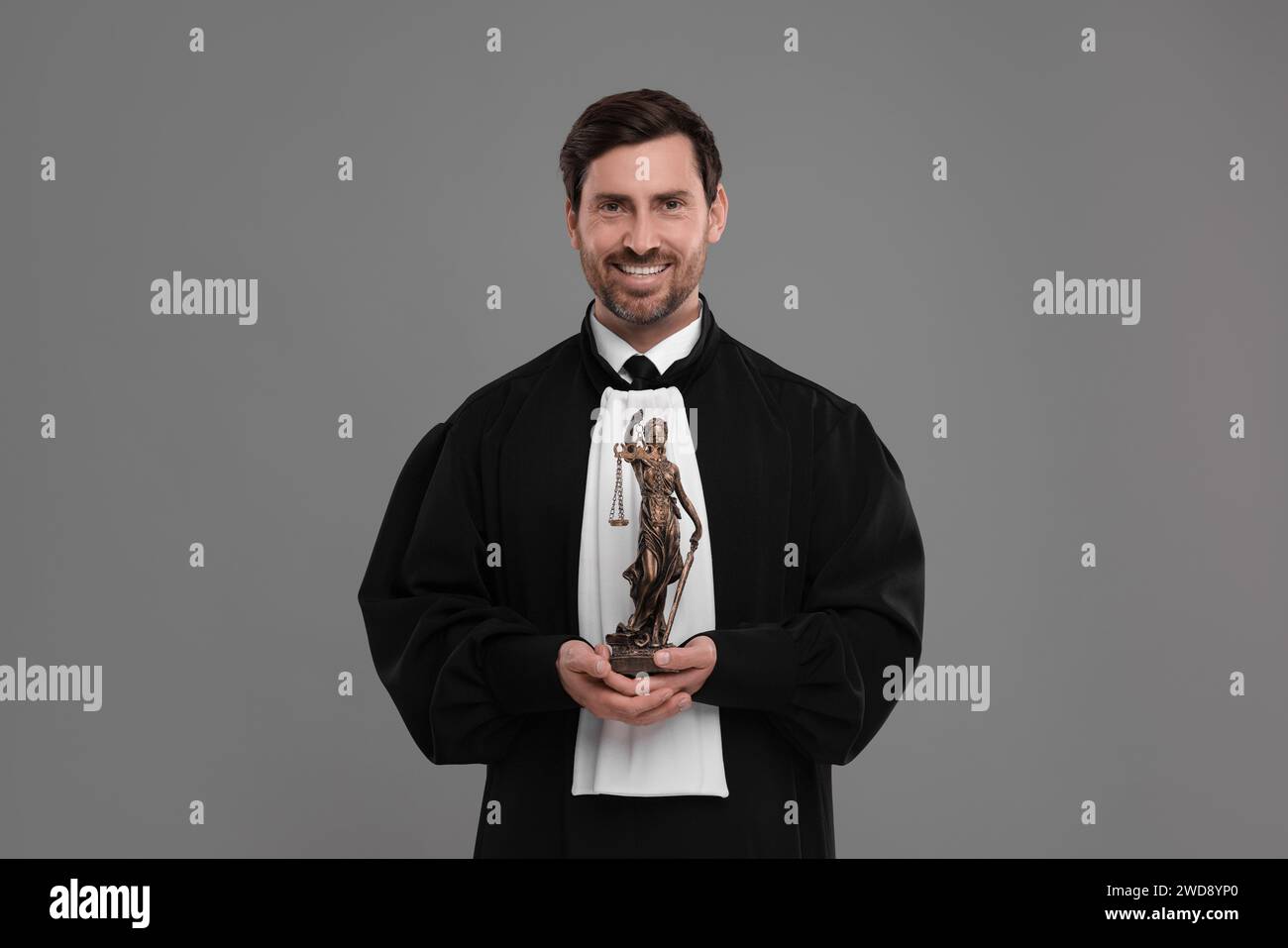 Smiling judge with figure of Lady Justice on grey background Stock ...