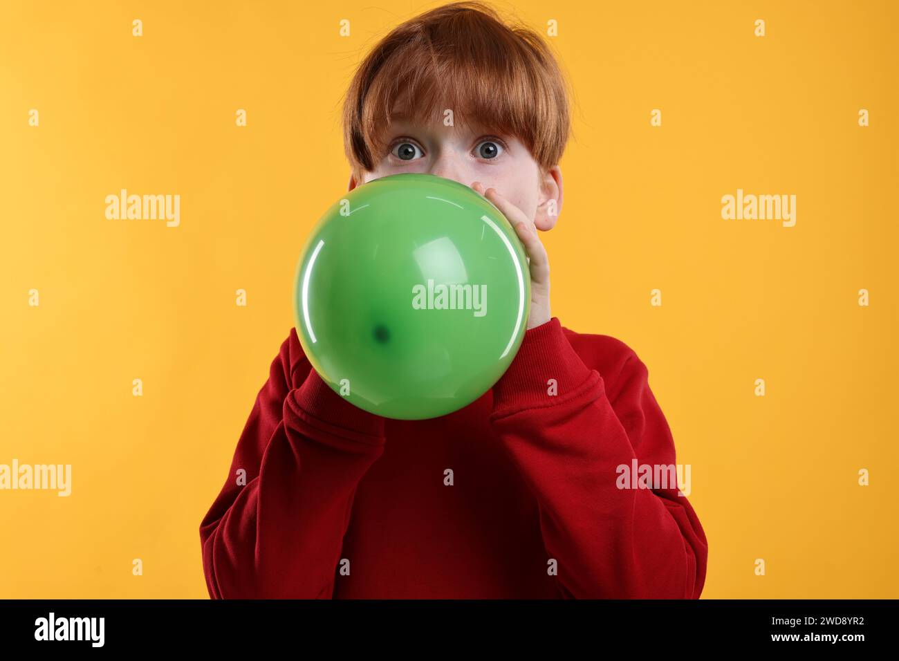 Boy inflating green balloon on orange background Stock Photo - Alamy