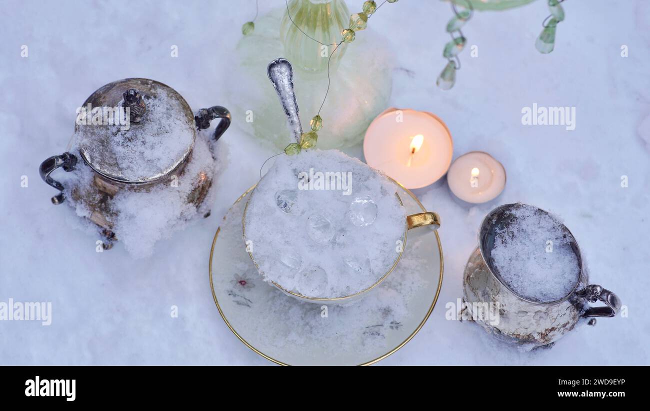 A cup filled with ice in the snow. Glass crystals. Lit tea lights. A ...