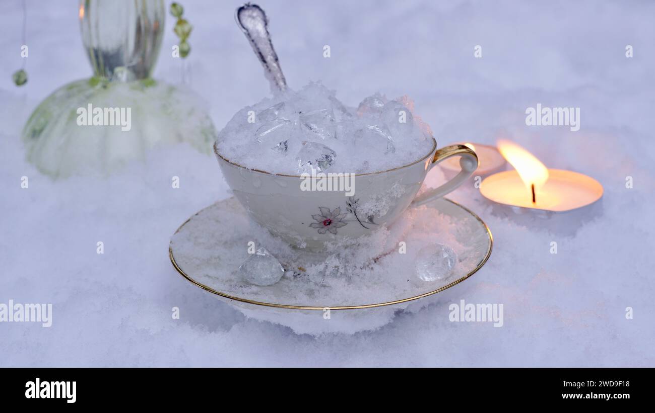 A cup filled with ice in the snow. Glass crystals. Lit tea lights ...
