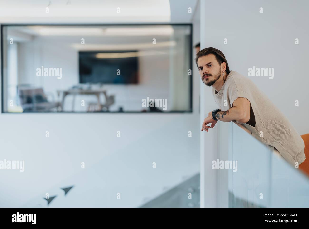A thoughtful man with a beard leans on a glass partition in a modern ...