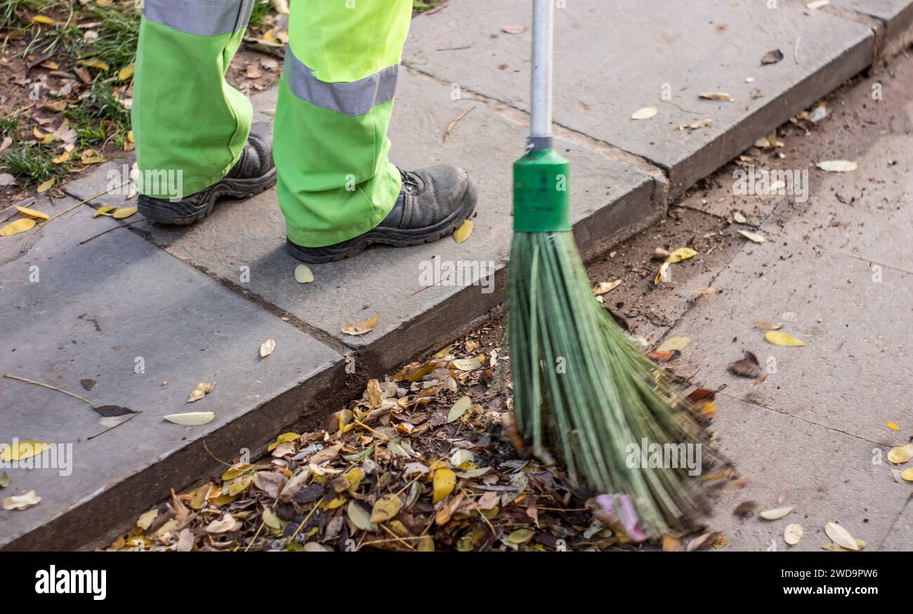 Municipal worker sweep the road with broomstick and collects garbage in ...
