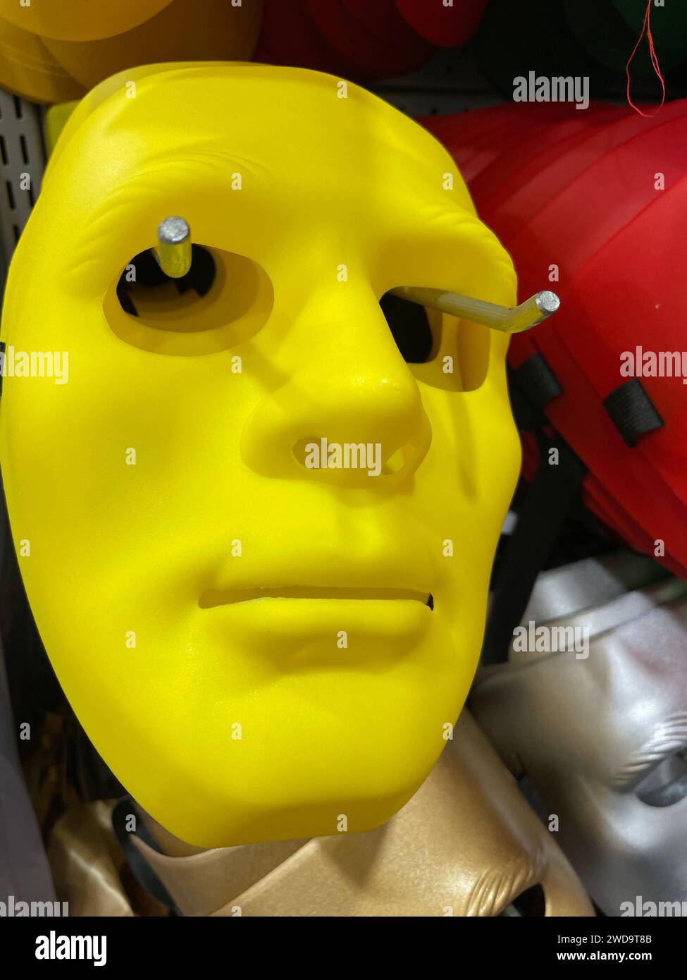 A bright yellow plastic mask on display, with metallic pins put into ...