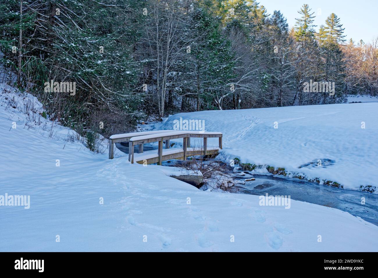 A wooden bridge covered with snow crossing over a frozen creek that is ...