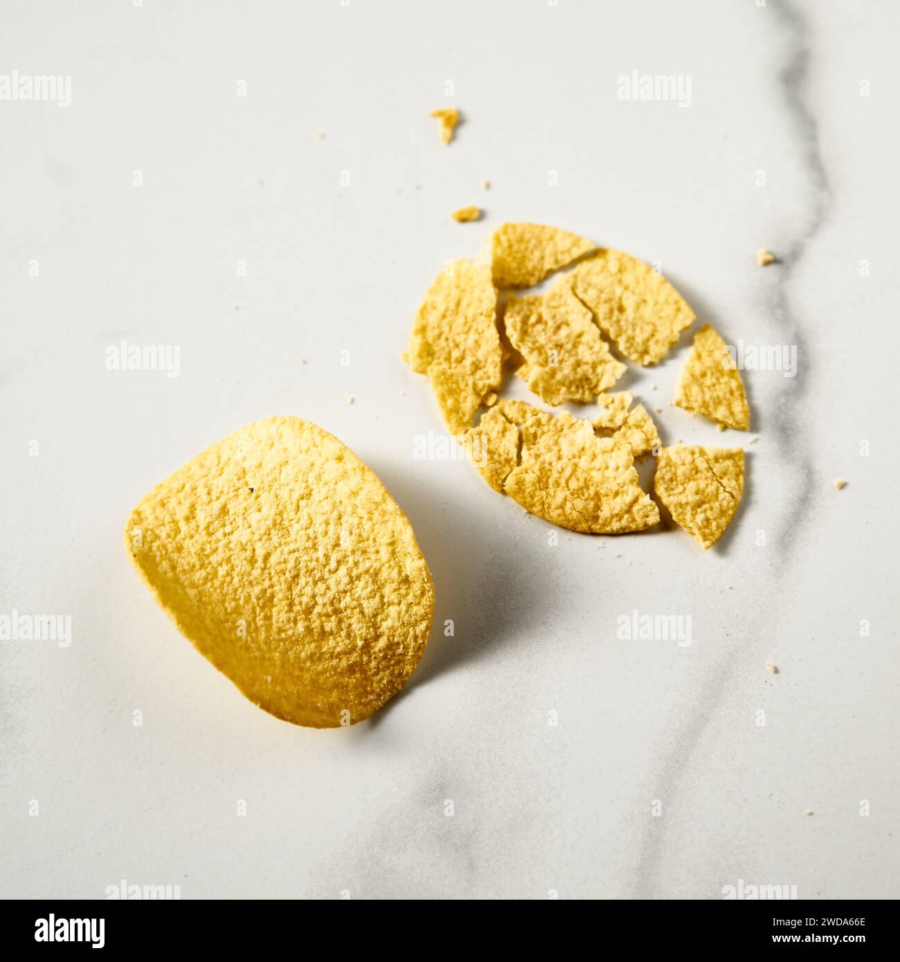 Pair of potato chips: whole and broken on white marble background ...