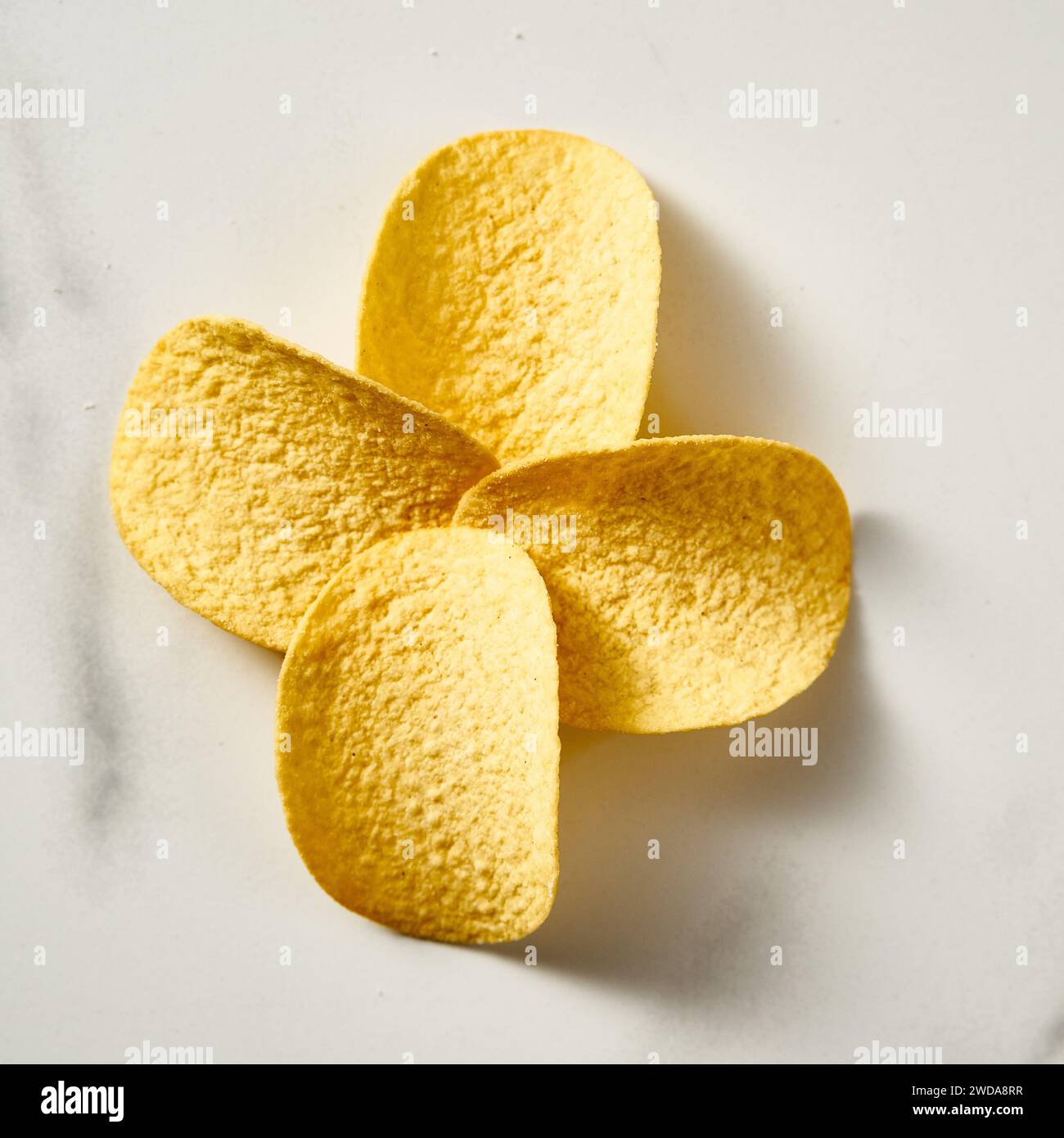 Four potato chips flower-shaped on white marble background ...