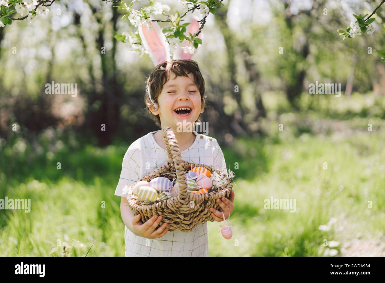 Funny boy with eggs basket and bunny ears on Easter egg hunt in sunny ...