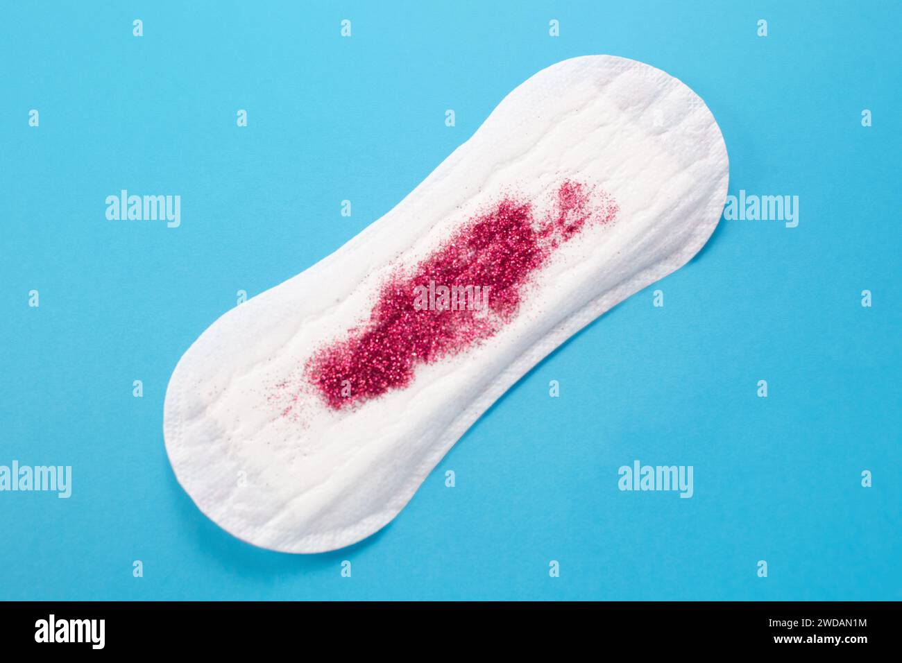 Feminine hygiene pad with red glitter on blue background. First ...