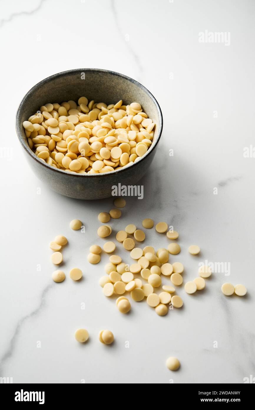 White chocolate drops in the bowl on white marble background. Baking ...